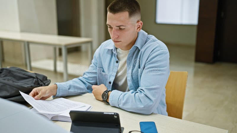 A Young Hispanic Man Studies Paperwork in a Brightly-lit College ...