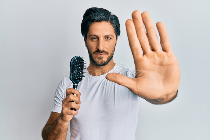 Young Hispanic Man Styling Hair Using Comb with Open Hand Doing Stop ...