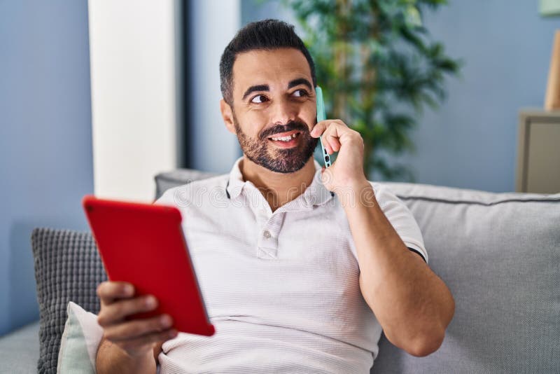 Young Hispanic Man Talking on the Smartphone Using Touchpad Sitting on ...