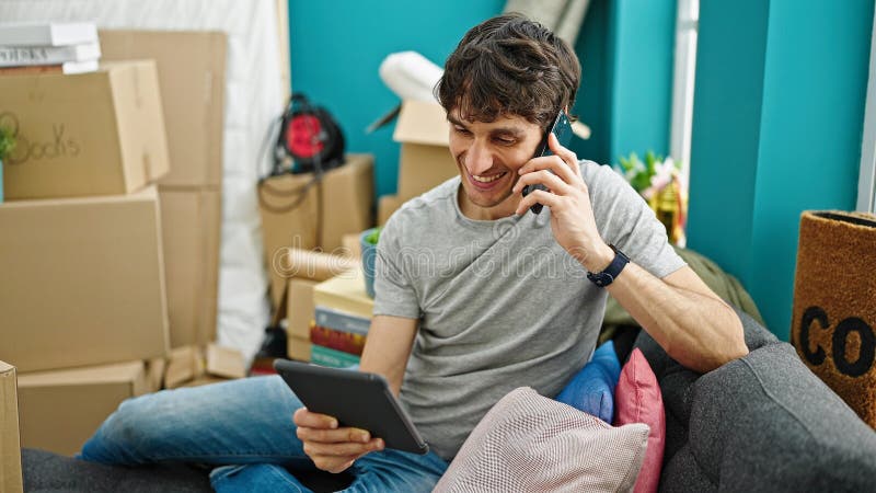 Young Hispanic Man Talking on Smartphone Using Touchpad Sitting on Sofa ...