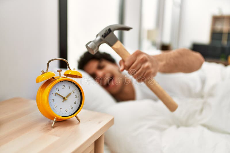 Young Hispanic Man Turning Off Alarm Clock Using Hammer Lying on the ...