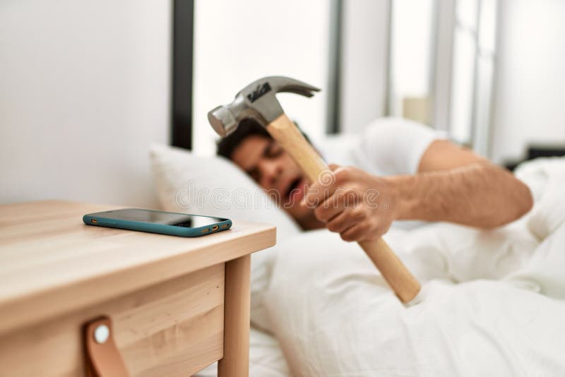 Young Hispanic Man Turning Off Alarm Clock Using Hammer Lying on the ...