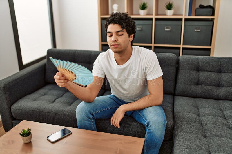 Young Hispanic Man Using Hand Fan Sitting on the Sofa at Home Stock ...