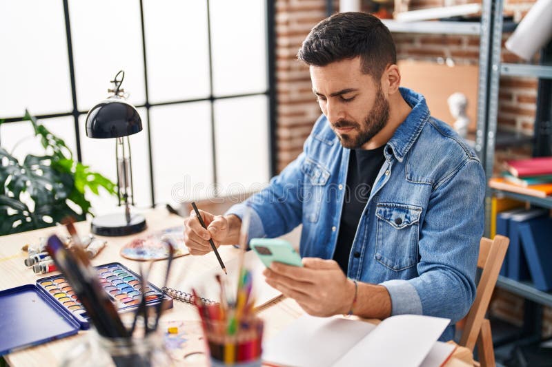 Young Hispanic Man Using Smartphone and Drawing Sitting on Table at Art ...