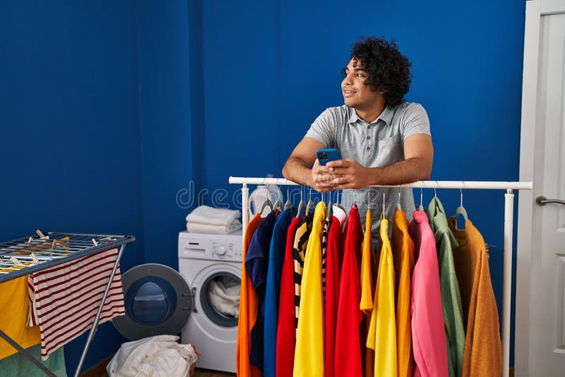 Young Hispanic Man Using Smartphone Leaning on Rack at Laundry Room ...