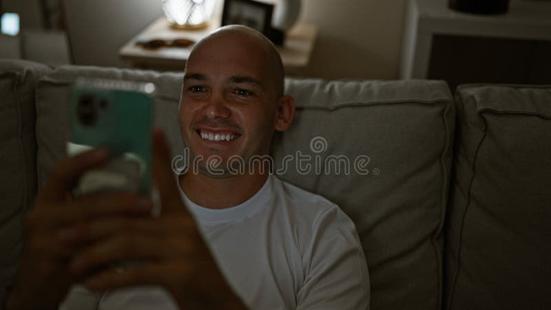 Young Hispanic Man Using Smartphone Sitting on Sofa Smiling at Home ...