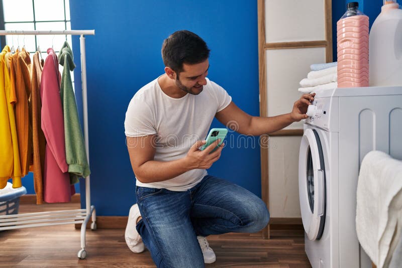 Young Hispanic Man Using Smartphone Turning on Washing Machine at ...