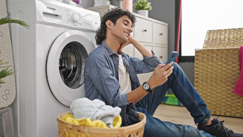 Young Hispanic Man Using Smartphone Waiting for Washing Machine at ...