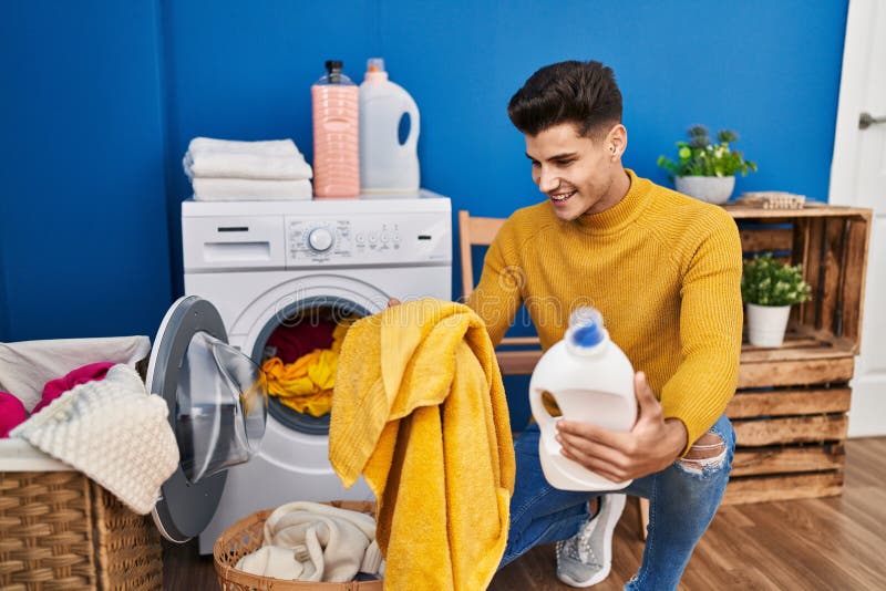 Young Hispanic Man Washing Clothes Holding Detergent Bottle at Laundry ...