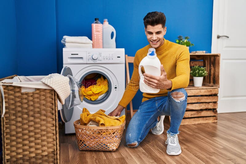 Young Hispanic Man Washing Clothes Holding Detergent Bottle at Laundry ...