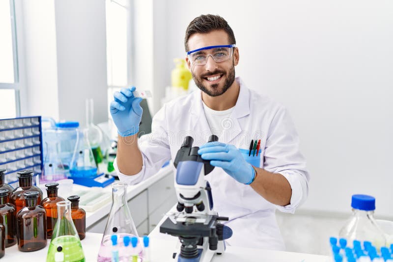 Young Hispanic Man Wearing Scientist Uniform Using Microscope at ... Young Hispanic Man Wearing Scientist Uniform Using Microscope at ...