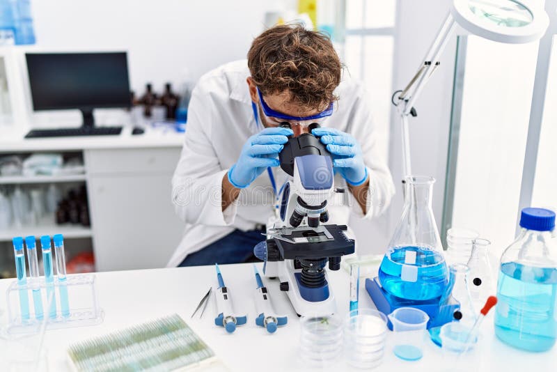 Young Hispanic Man Wearing Scientist Uniform Using Microscope at ...