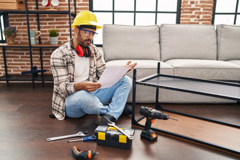 Young Hispanic Man Worker Reading Instructions Holding Wrench at Home ...