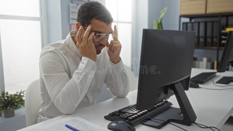 Young Hispanic Man Working in an Office, Concentrating on a Computer Screen with Glasses and a ...