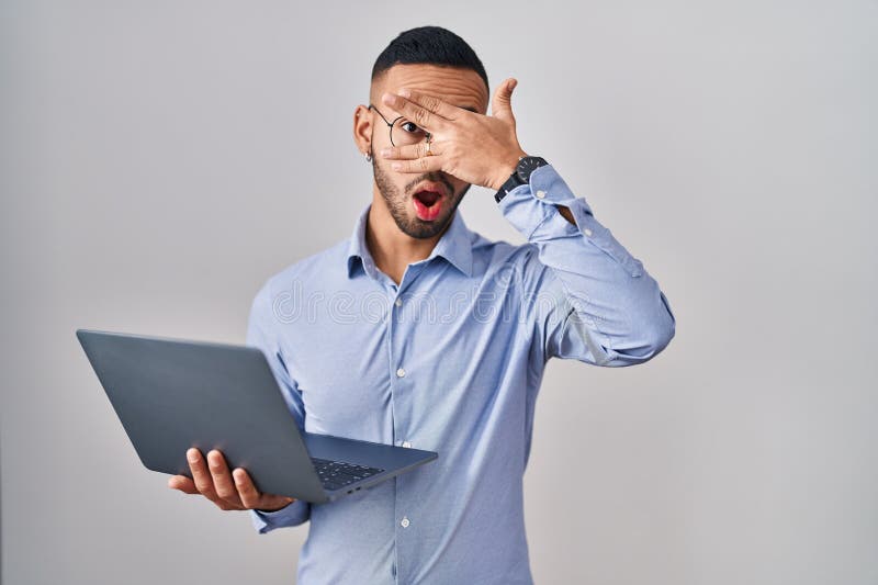 Young Hispanic Man Working Using Computer Laptop Peeking in Shock ...