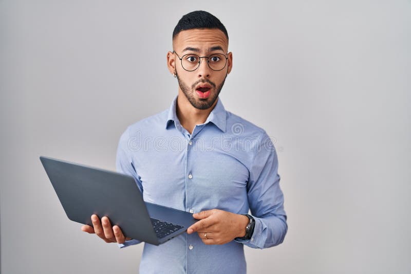 Young Hispanic Man Working Using Computer Laptop in Shock Face, Looking ...