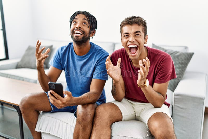 Young Hispanic Men Using Smartphone Sitting on the Sofa at Home Crazy ...