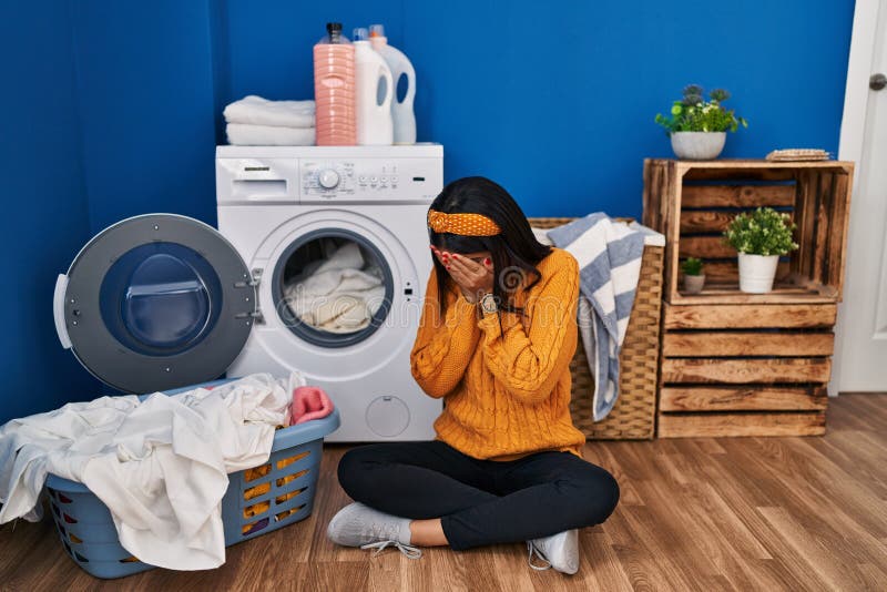 Young Hispanic Woman Doing Laundry with Sad Expression Covering Face ...