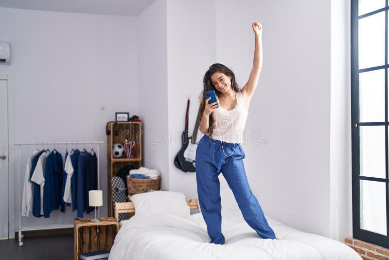Young Hispanic Woman Listening To Music And Dancing On Bed At Bedroom