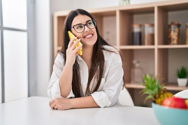 Young Hispanic Woman Talking on the Smartphone Sitting on Table at Home ...