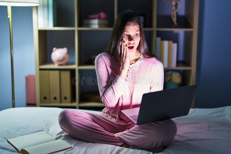 Young Hispanic Woman Using Computer Laptop on the Bed Afraid and ...