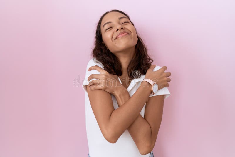 Young Hispanic Woman Wearing Casual White T Shirt Hugging Oneself Happy