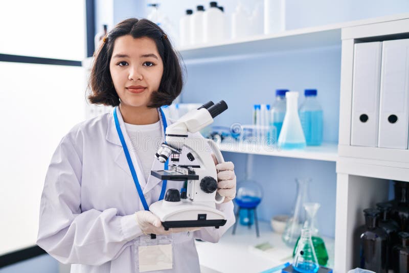 Young Hispanic Woman Working at Scientist Laboratory Holding Microscope ...