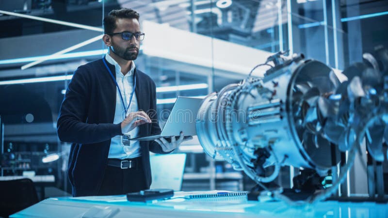 Young Industrial Engineer Working on a Futuristic Jet Engine, Standing ...