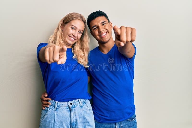 Young Interracial Couple Wearing Casual Clothes Pointing To You And The