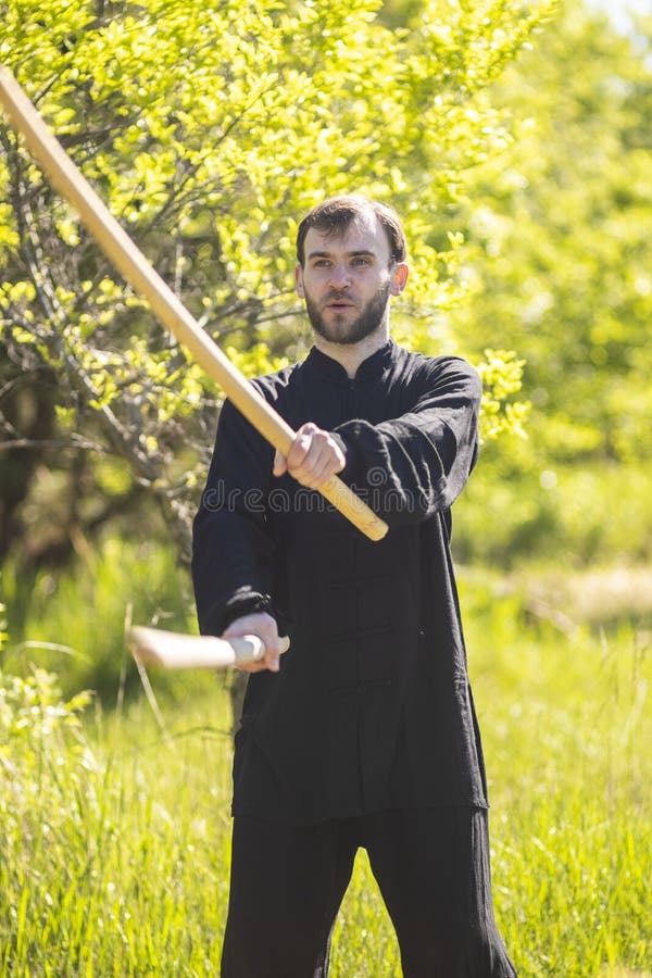 A Young Karate Guy is Engaged in Wushu with Weapons in the Park ...