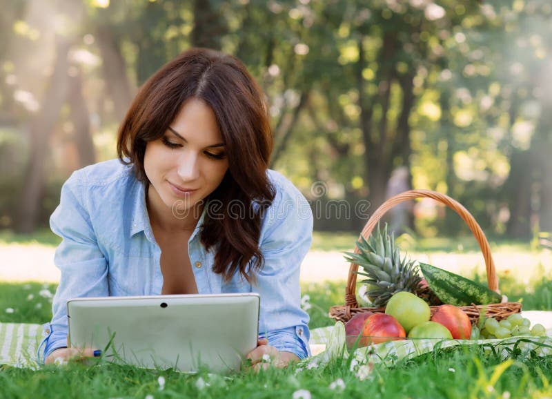 Young Lady Lying on a Mat in the Park Browsing Her Tablet Stock Photo ...