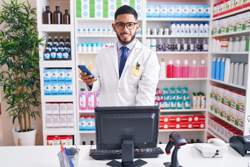 Young Latin Man Pharmacist Using Smartphone and Computer at Pharmacy ...