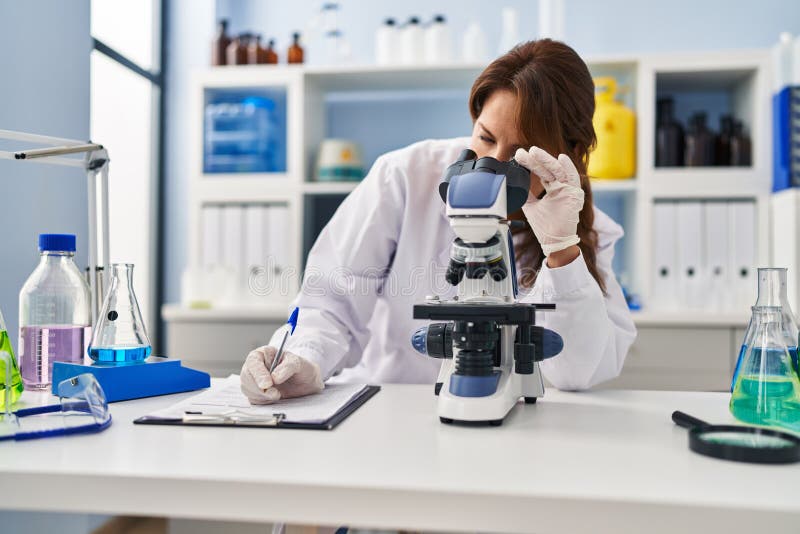 Young Latin Woman Wearing Scientist Uniform Using Microscope Writing on ...