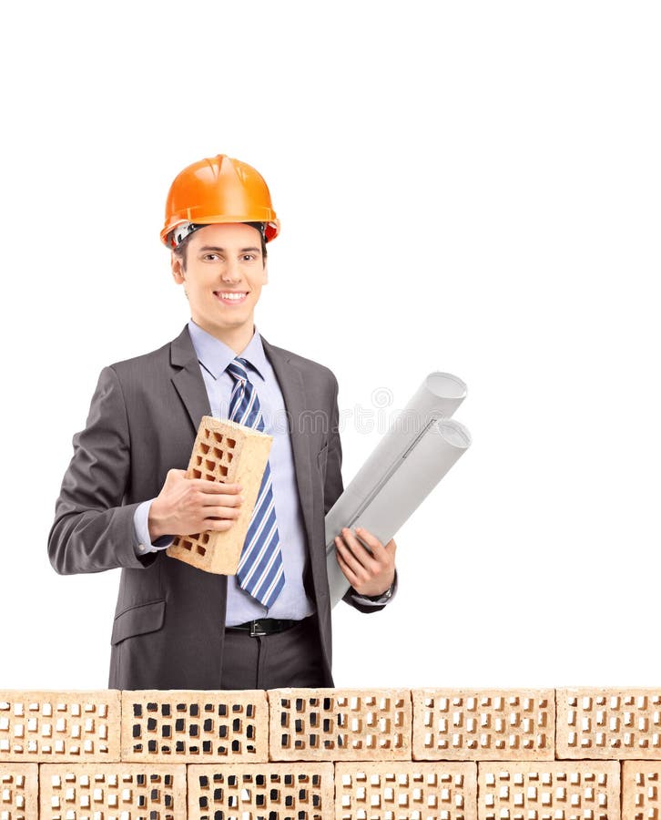 Young Male Engineer Holding a Brick and a Blueprint Behind Brick Stock ...