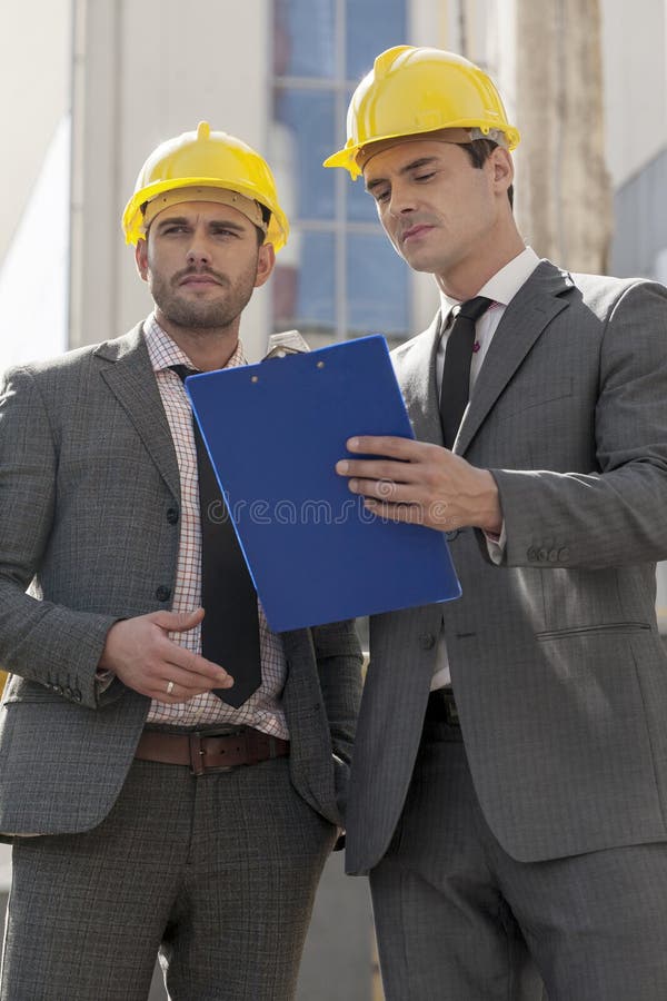 Young Male Engineers with Clipboard Discussing at Construction Site ...