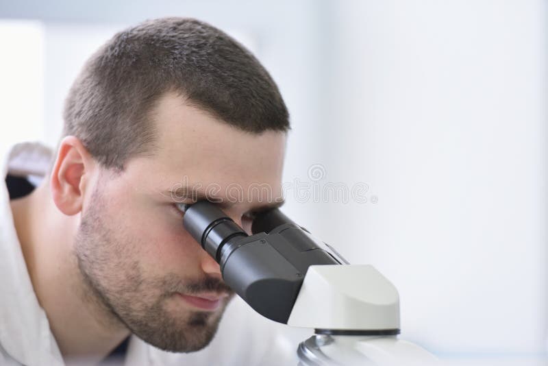 Young Male Scientist Looking through a Microscope in a Laboratory Doing ...