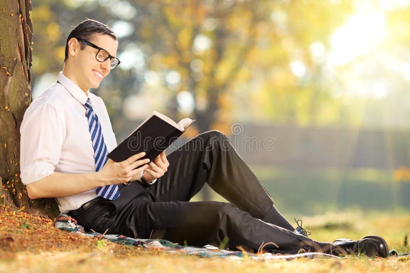 Young Male Sitting on Green Grass and Reading Book in Park Stock Photo ...