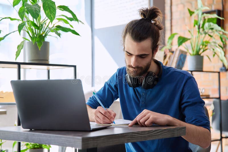 Young Male University Student Studying Using Laptop, Writing in ...