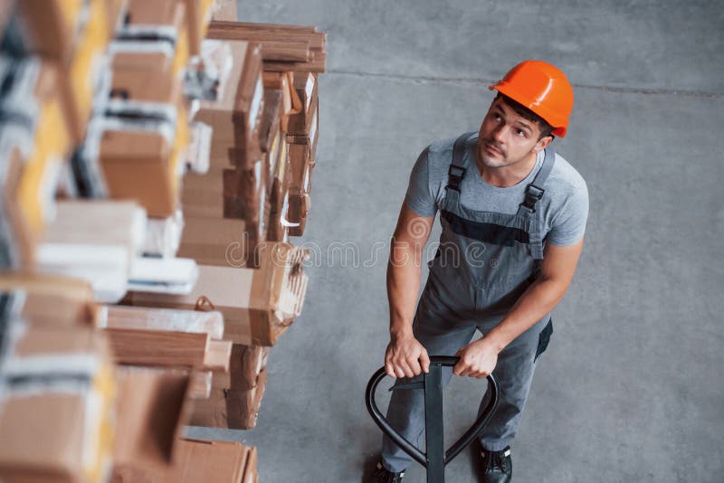 Young Male Worker in Uniform is in the Warehouse with Pallet Truck ...