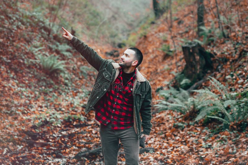 Young Man in Autumn Forest with Raised Hand Showing Something on Cliff ...