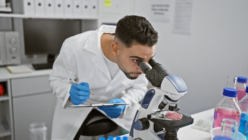A Young Man with a Beard Examines Samples Under a Microscope in a ...