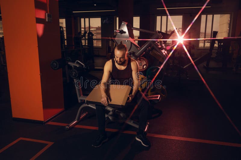 A Young Man with a Beard with a Happy Face Opens a Pizza Box in the Gym ...