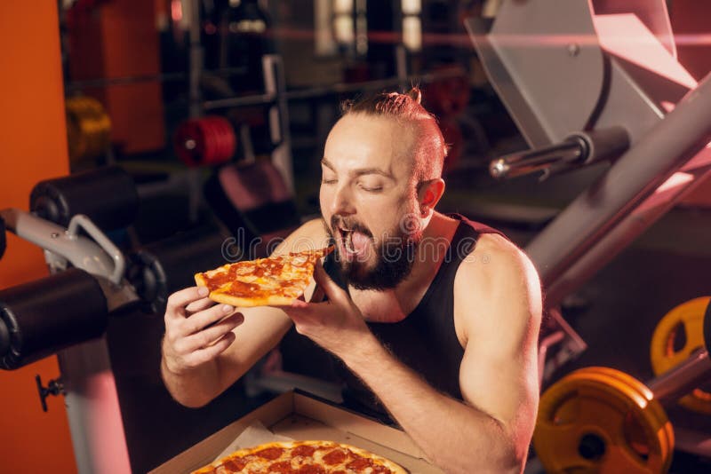 A Young Man with a Beard is Happy To Eat Pizza in the Gym Stock Photo ...