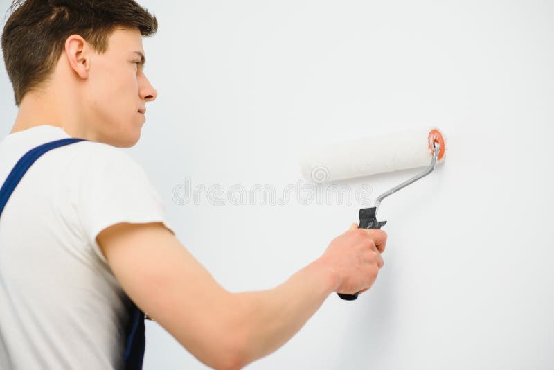 Young Man in Blue Overalls Painting Wall into White Color with a Roller ... Young Man in Blue Overalls Painting Wall into White Color with a Roller ...
