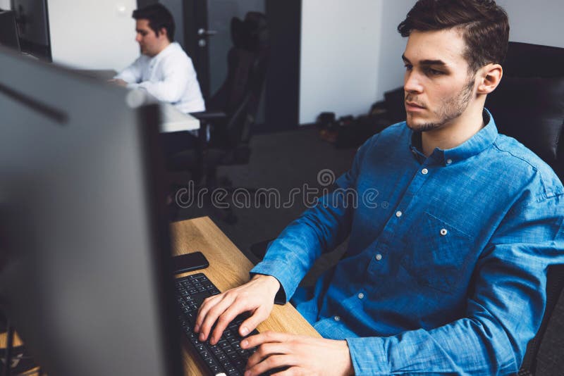 Young Man In A Blue Shirt A Programmer Typing On Keyboard While Looking