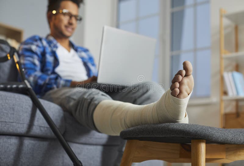 Young Man with Broken Leg Sitting on Sofa Using Laptop Stock Photo ...