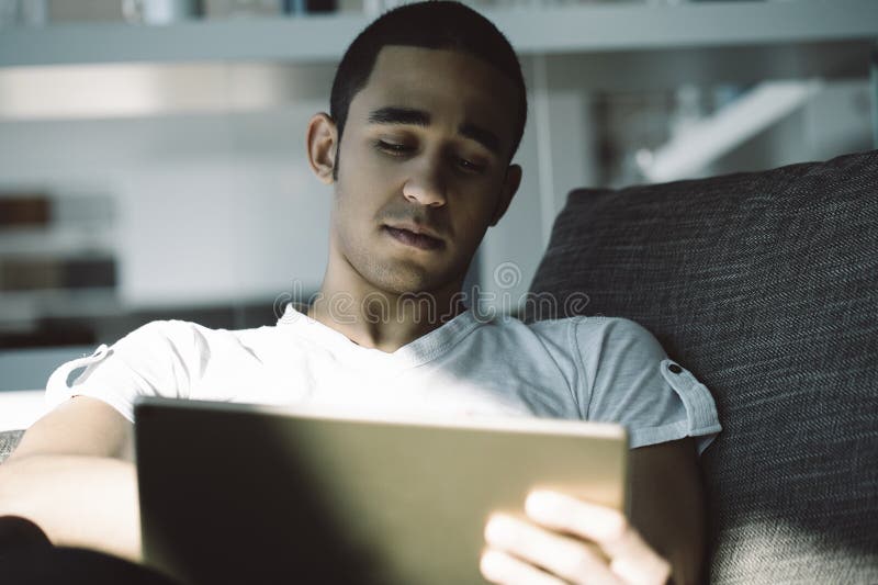 Young Man Browsing the Internet on Tablet while Relaxing on Sofa Stock ...
