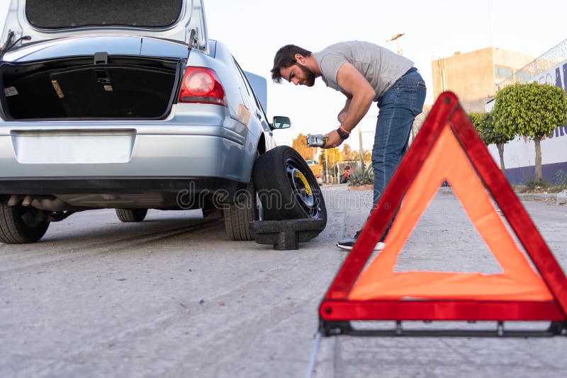 Young Man Changing a Flat Tire on the Road, Using a Hazard Triangle ... Young Man Changing a Flat Tire on the Road, Using a Hazard Triangle ...