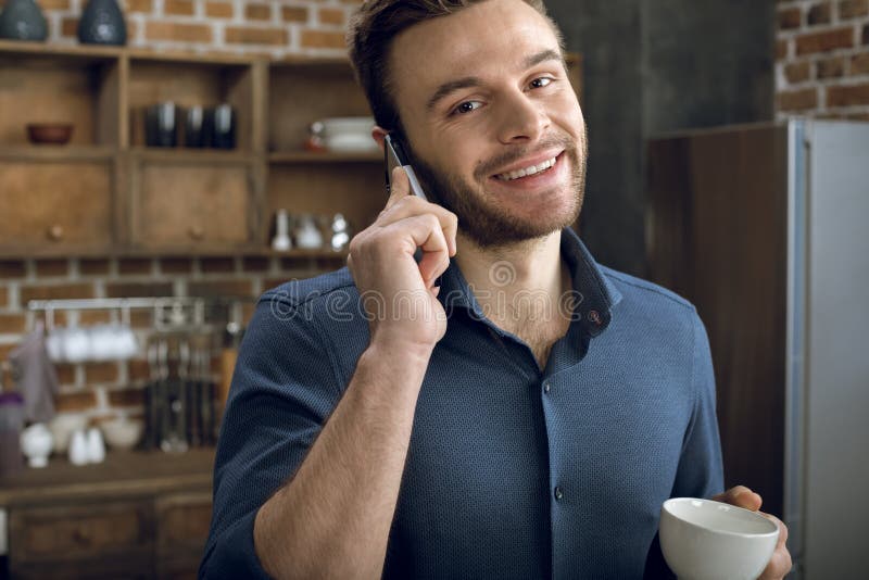 Young Man with Coffee Cup Talking on Smartphone and Smiling at Camera ...