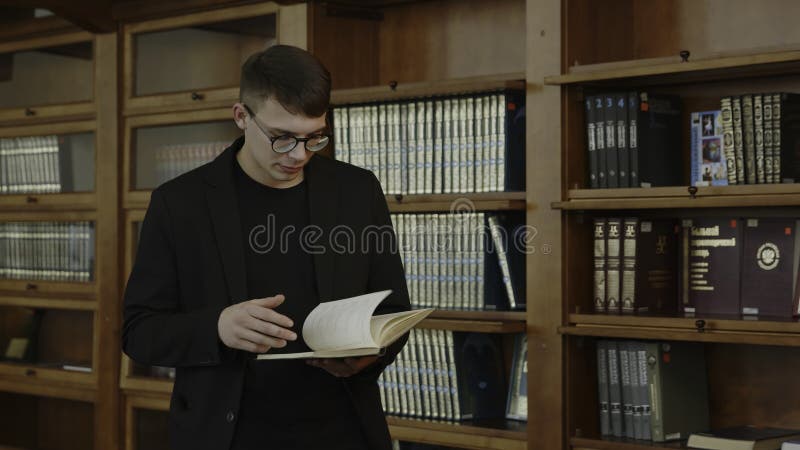 A Young Man is Deep in Reading a Book in a Library, Surrounded by ...